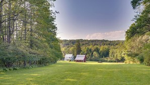 Paisagem rural com um campo gramado, um celeiro vermelho e uma casa branca.