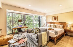 Quarto moderno com uma cama grande, uma escrivaninha e vista para o verde pelas janelas.