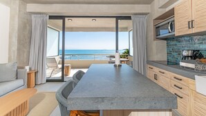 Uma cozinha moderna com uma ilha grande, armários de madeira e vista para o oceano.