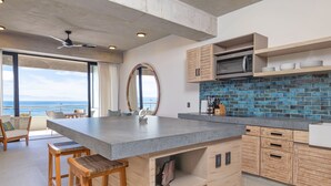 Uma cozinha moderna com uma ilha grande, armários de madeira e vista para o oceano.