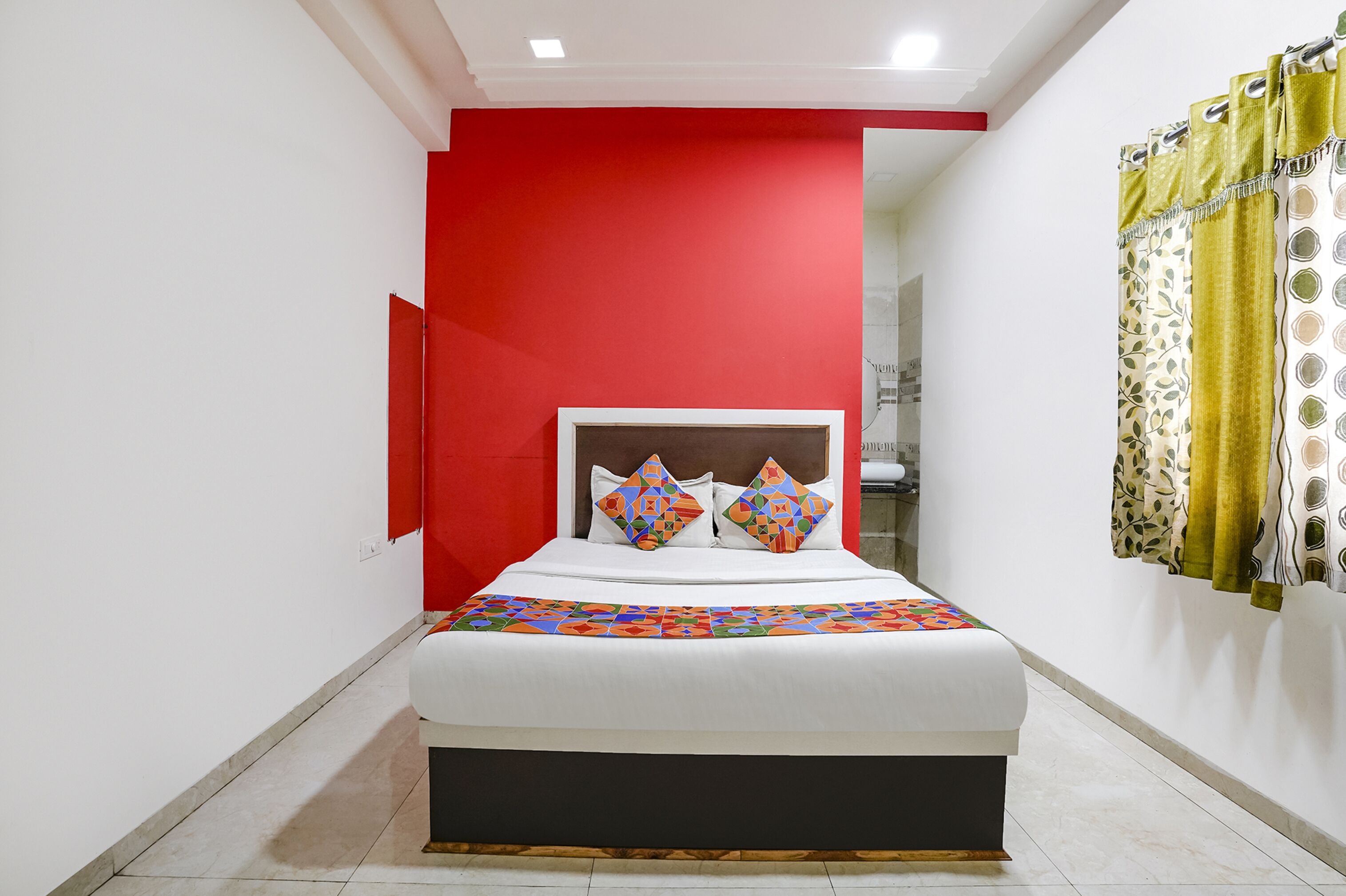 Quarto com cama, parede de destaque vermelha e colcha estampada.
