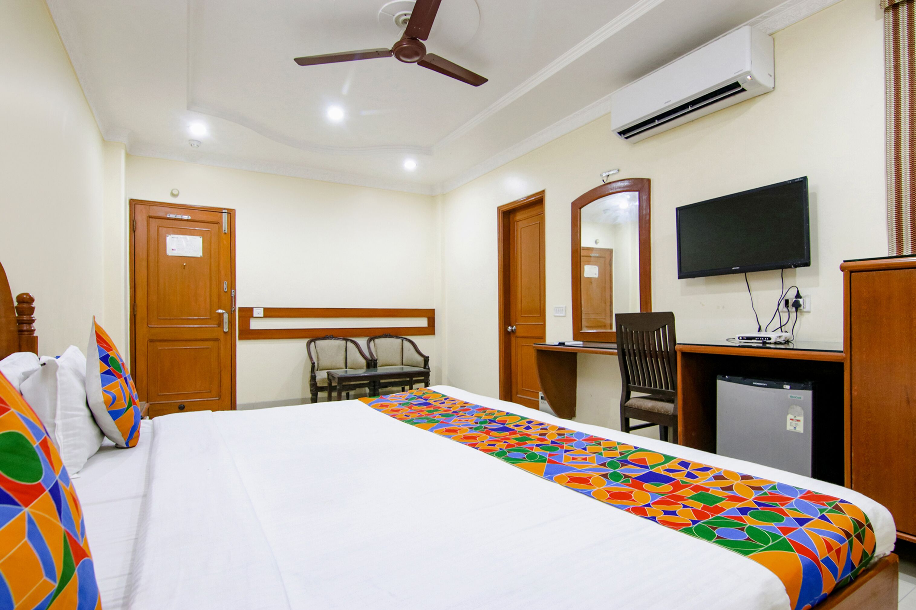 Quarto de hotel com cama, escrivaninha com computador, cadeira, televisão e ar condicionado.