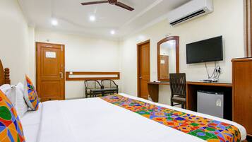 Quarto de hotel com cama, escrivaninha com computador, cadeira, televisão e ar condicionado.