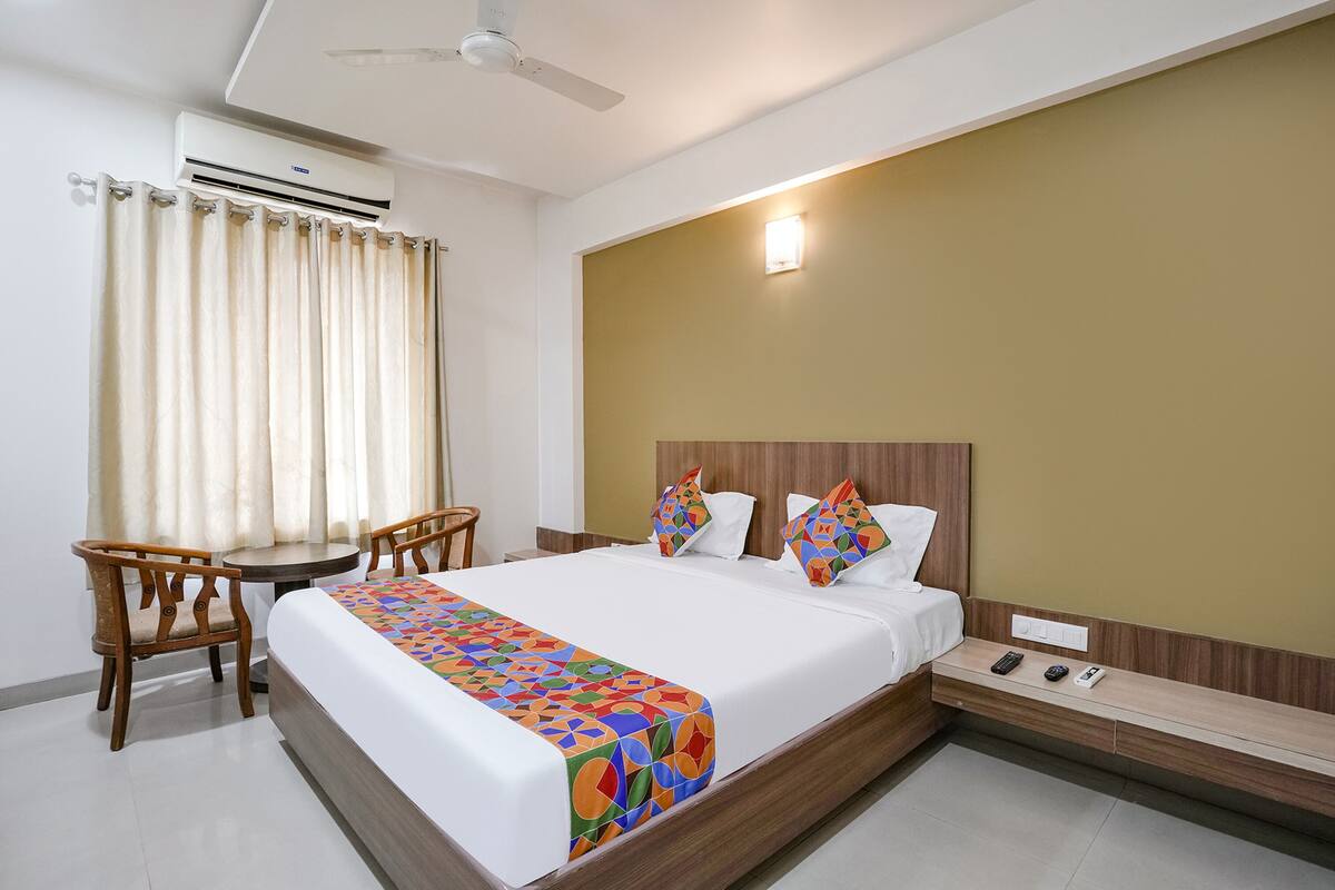 Quarto de hotel com cama, mesa de cabeceira, cadeira e aparelho de ar condicionado.