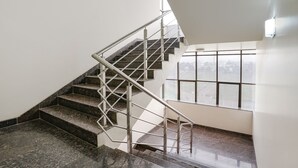 Uma escadaria com guarda-corpos de metal e degraus de granito que leva a um patamar com grandes janelas.