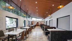 Uma sala de jantar ampla, com pé direito alto, janelas grandes e piso estampado.
