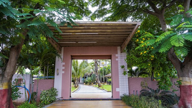 Uma galeria coberta com um caminho que leva a um edifício, rodeado por vegetação e árvores.