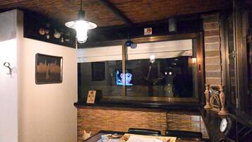 Interior de restaurante com teto de madeira, janela com vista, mesa com cardápios e relógio fixado na parede.