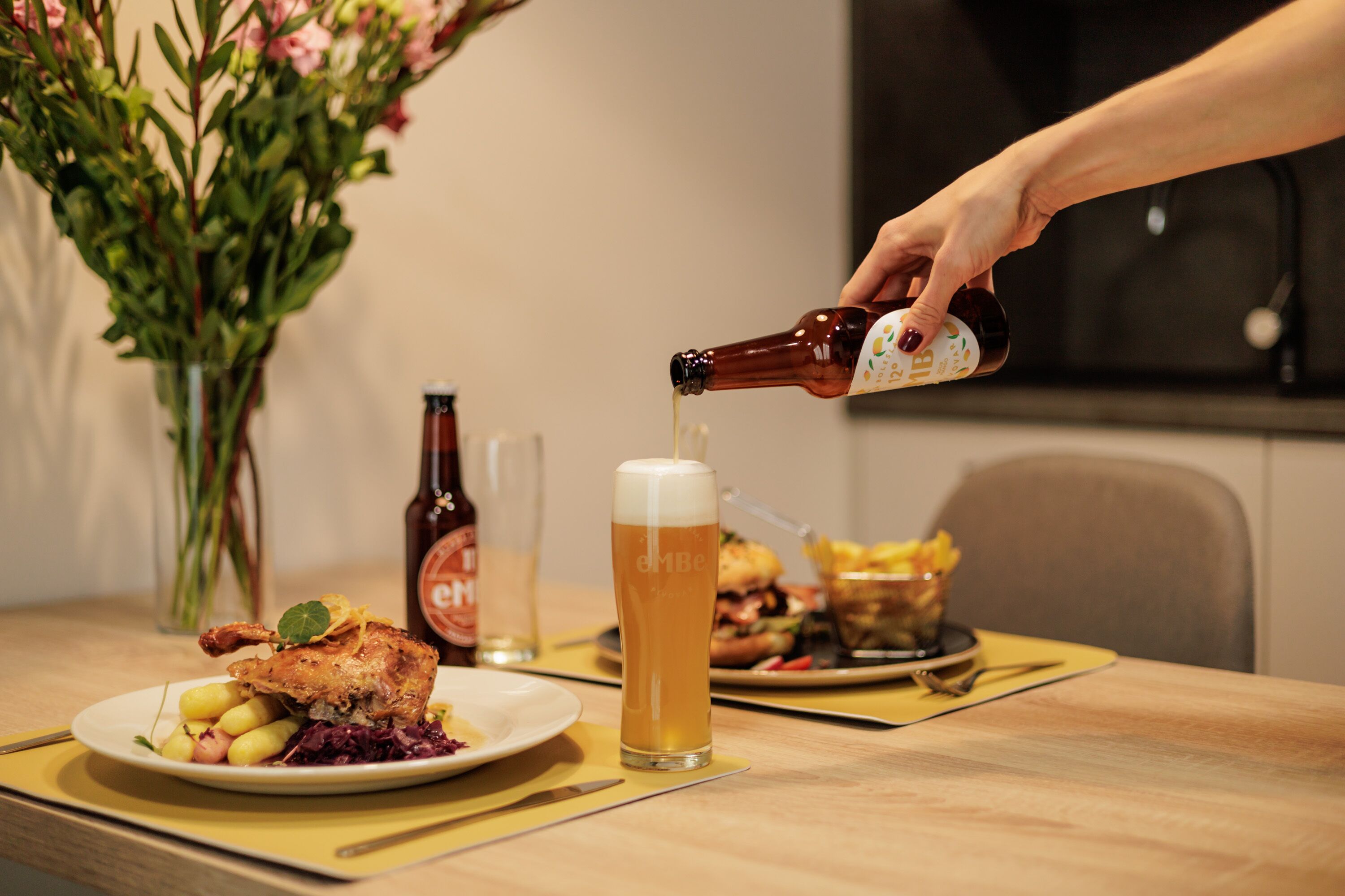 Uma mesa de jantar com um prato de comida, um copo de cerveja e uma garrafa sendo servida no copo.