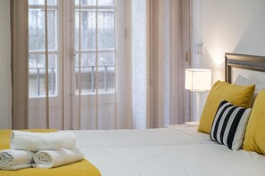 Quarto de hotel com cama, luminária e janela com cortinas.