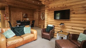 Interior de uma cabana de madeira com sofá e poltronas de couro, uma pequena mesa de madeira e uma televisão montada na parede.