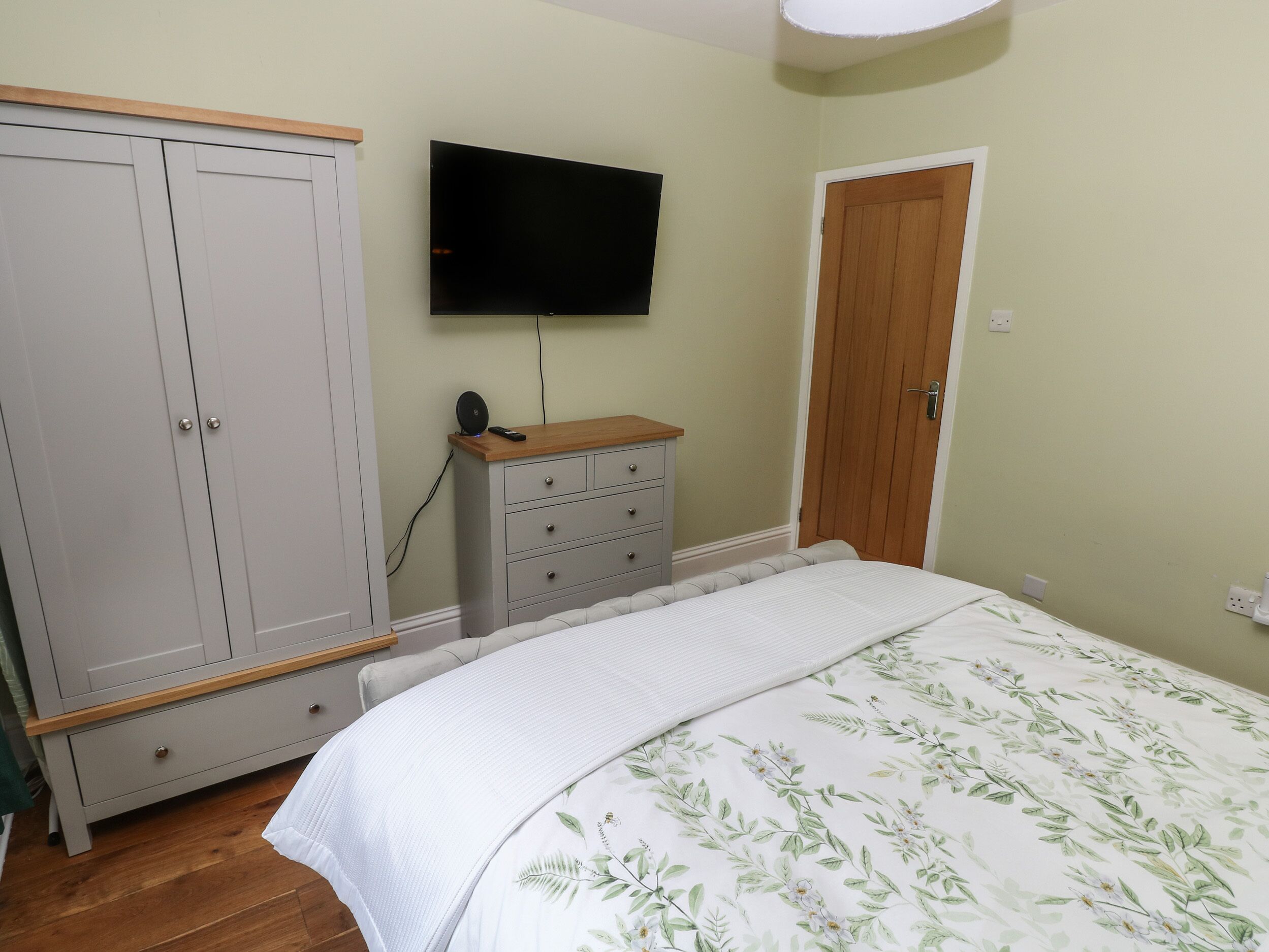 Quarto com cama, guarda-roupa, penteadeira, televisão na parede e porta.
