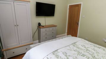 Quarto com cama, guarda-roupa, penteadeira, televisão na parede e porta.