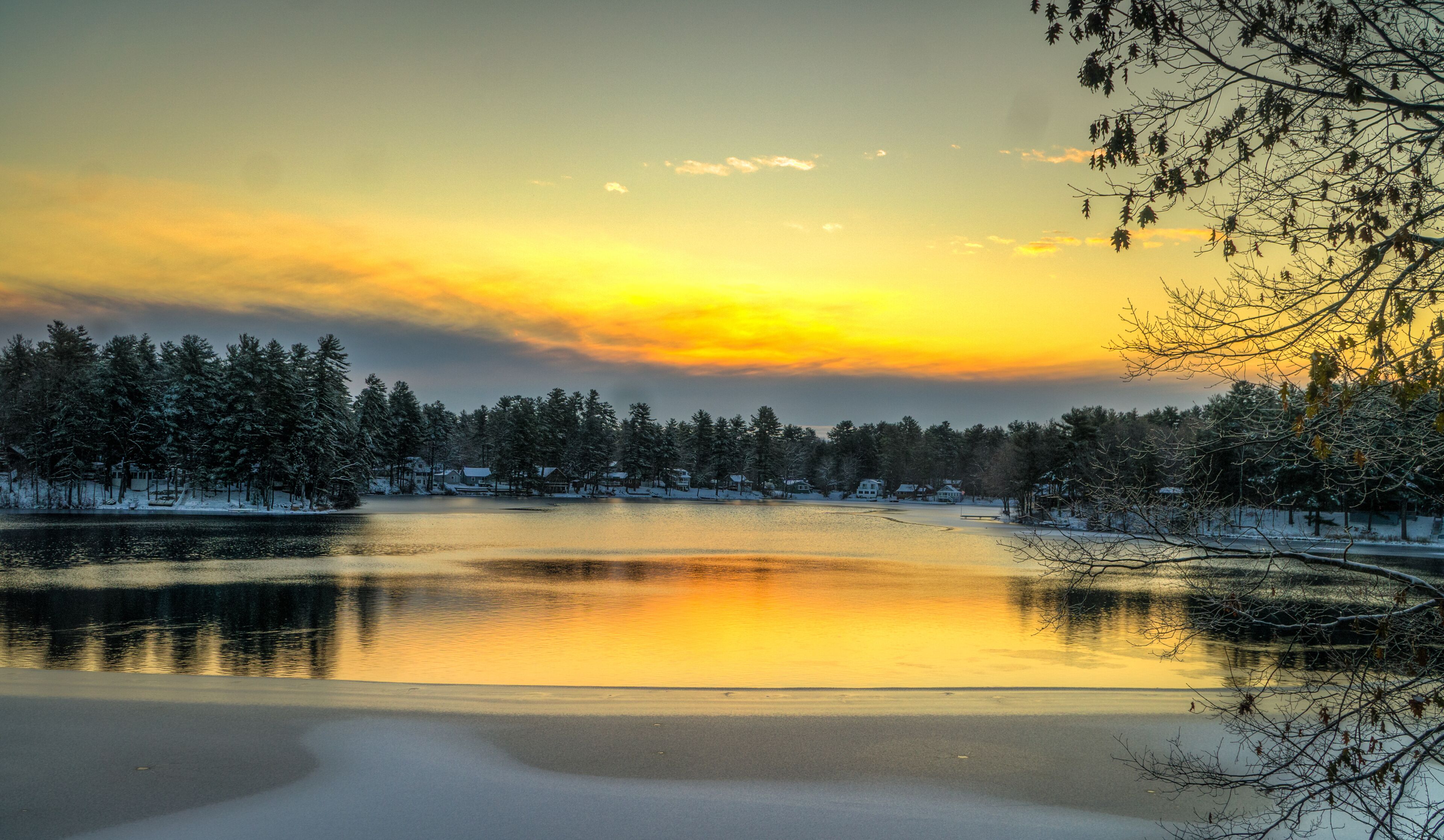Um lago congelado rodeado por árvores e casas cobertas de neve ao pôr do sol.