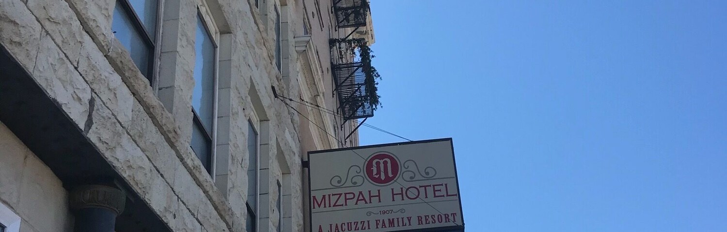 Um edifício histórico com uma placa para o Mizpah Hotel, fachada em estuque e uma montanha ao fundo.