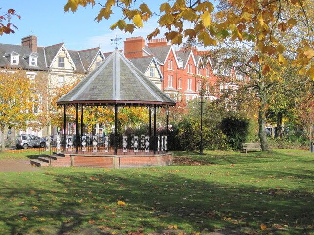 Um gazebo em um parque com folhas de outono, cercado por casas de tijolos vermelhos.