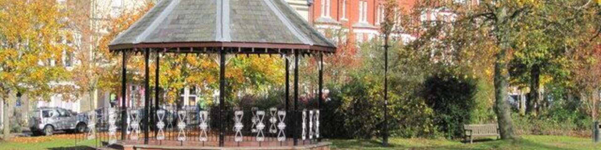 Um gazebo em um parque com folhas de outono, cercado por casas de tijolos vermelhos.