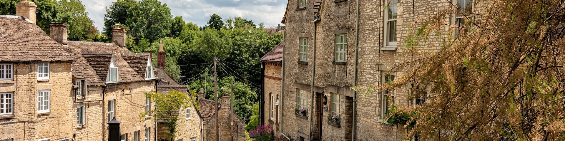 Uma vila charmosa com edifícios de pedra, um pátio gramado e vegetação exuberante.