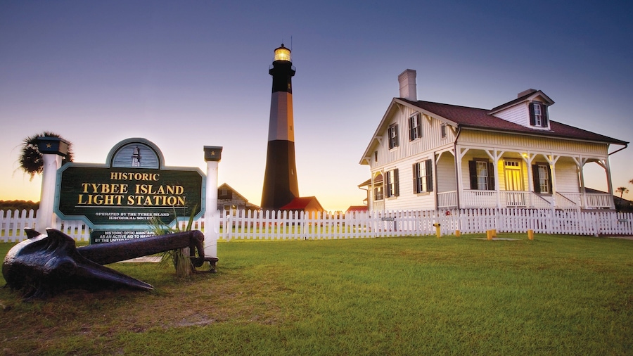 Um farol histórico e uma casa branca com varanda, cercados por uma cerca branca de piquete.