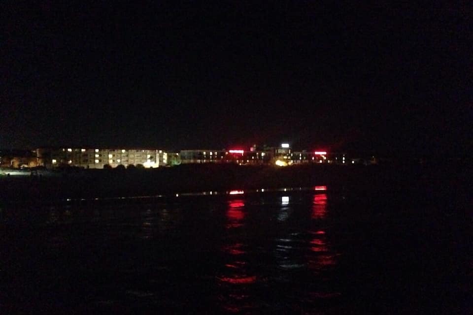 Vista noturna de uma orla com edifícios iluminados refletindo na água.