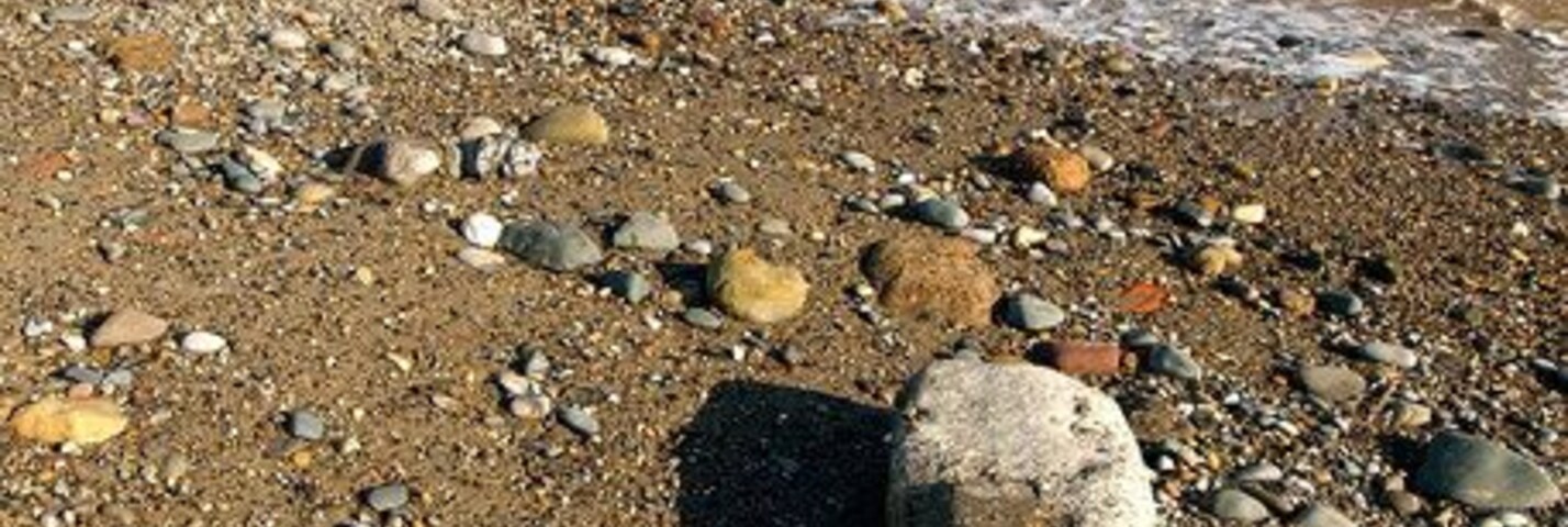 Uma praia rochosa com uma grande estrutura de pedra e uma formação semelhante a uma gruta ao fundo.
