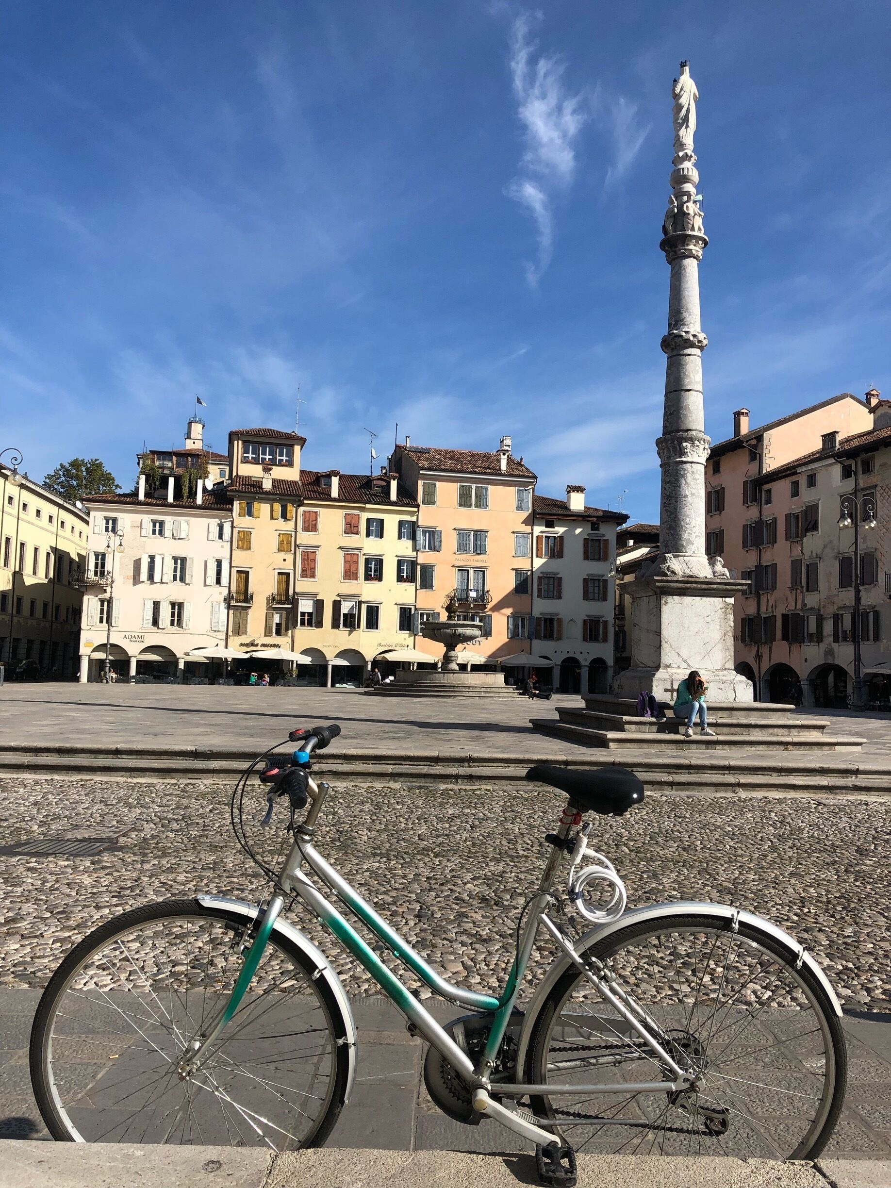 Uma bicicleta em praça com uma fonte e uma estátua ao fundo.