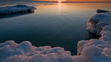 Lago congelado ao pôr do sol, com formações de gelo e céu limpo.