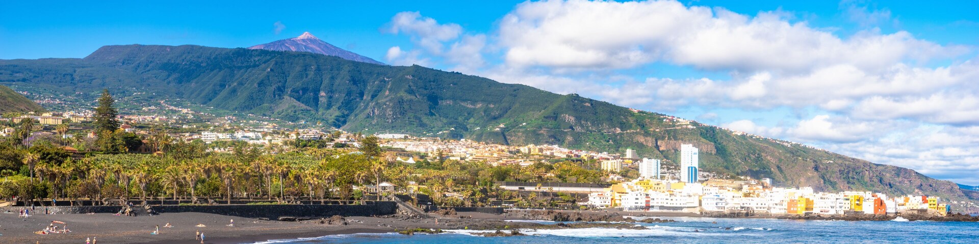 Uma cidade costeira com uma montanha ao fundo, uma praia e edifícios coloridos.