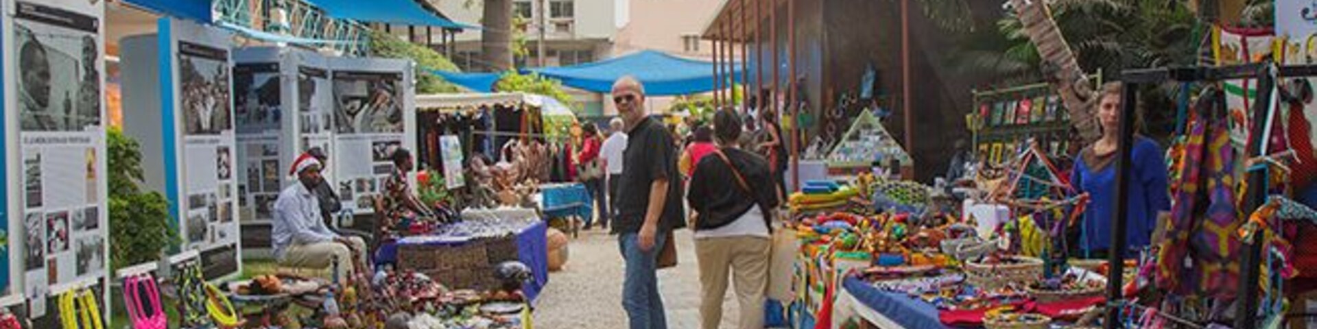 Um mercado ao ar livre movimentado, com barracas vendendo tecidos e artesanato coloridos.