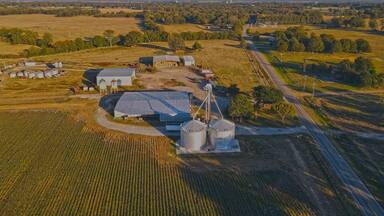 Vista aérea de uma fazenda rural com celeiros, silos e uma estrada.