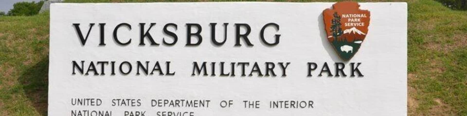Placa indicativa do Parque Militar Nacional de Vicksburg, com um canhão ao fundo.