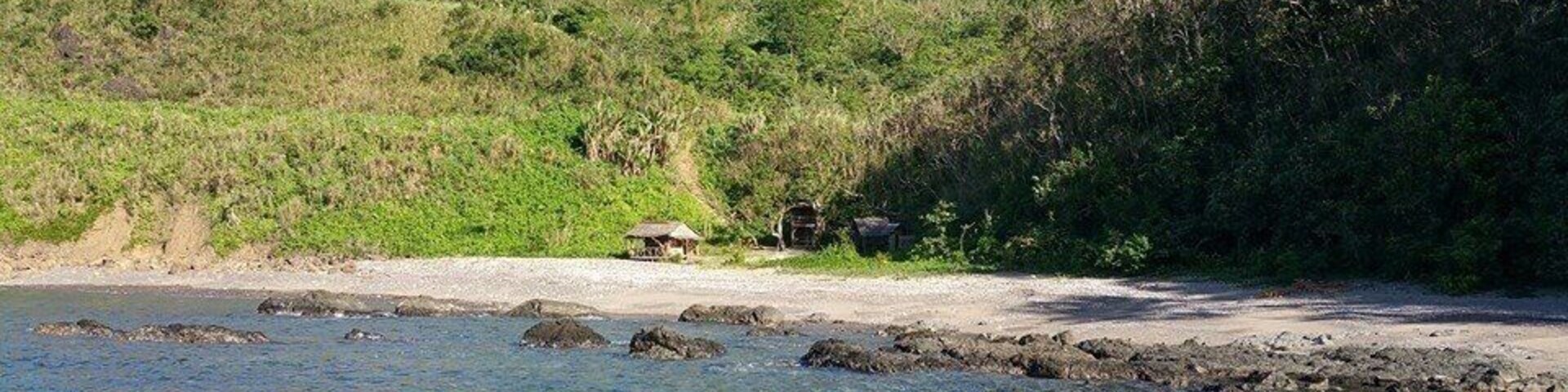 Uma praia com águas cristalinas, rochas e uma cabana na costa.