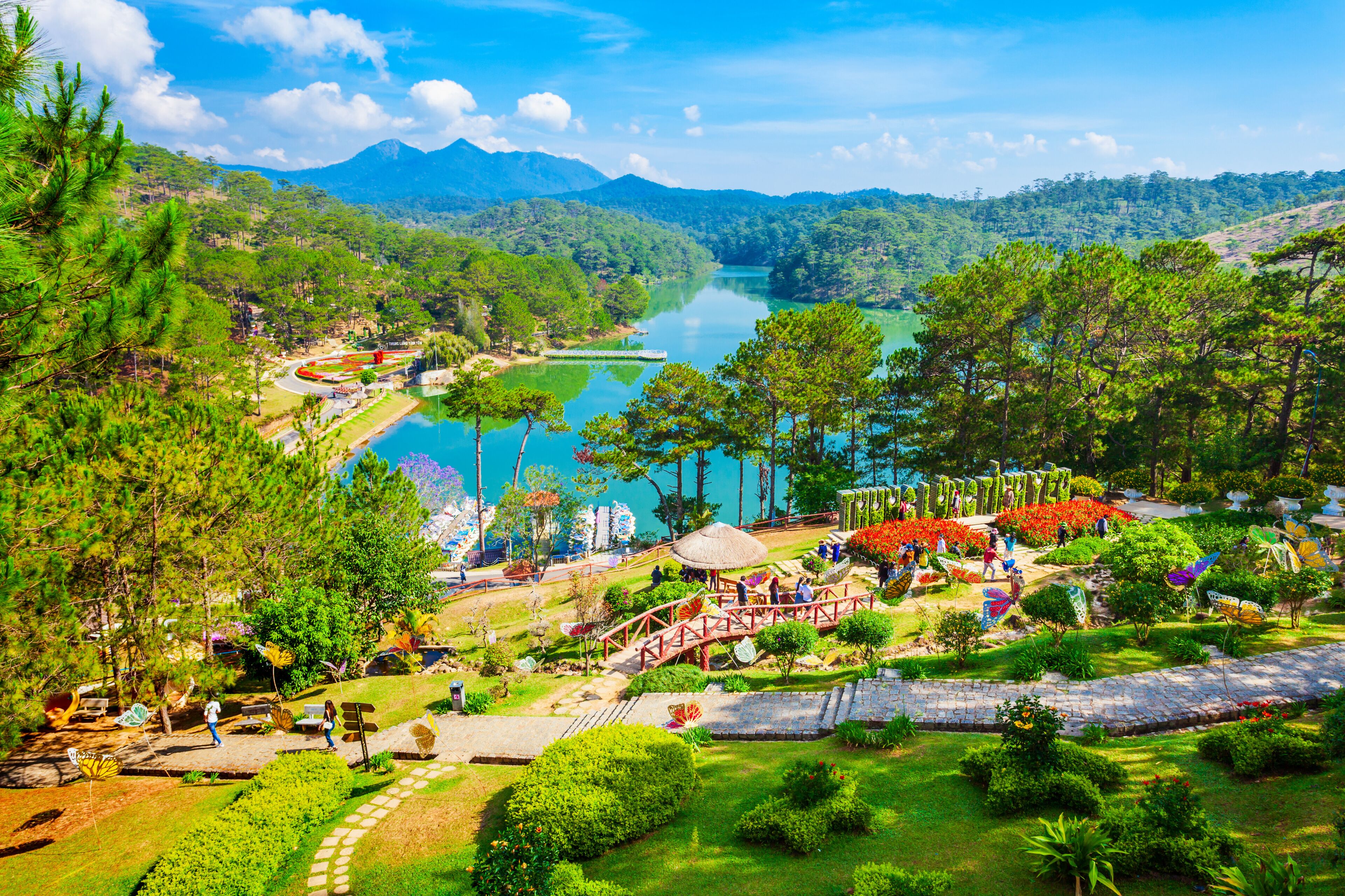 Paisagem exuberante com um rio, uma ponte e um parque com diversas plantas e árvores.