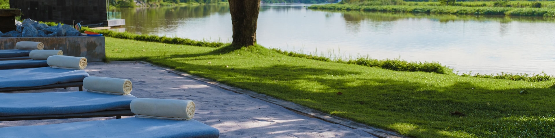 Uma área de relaxamento à beira do lago com espreguiçadeiras e uma árvore.