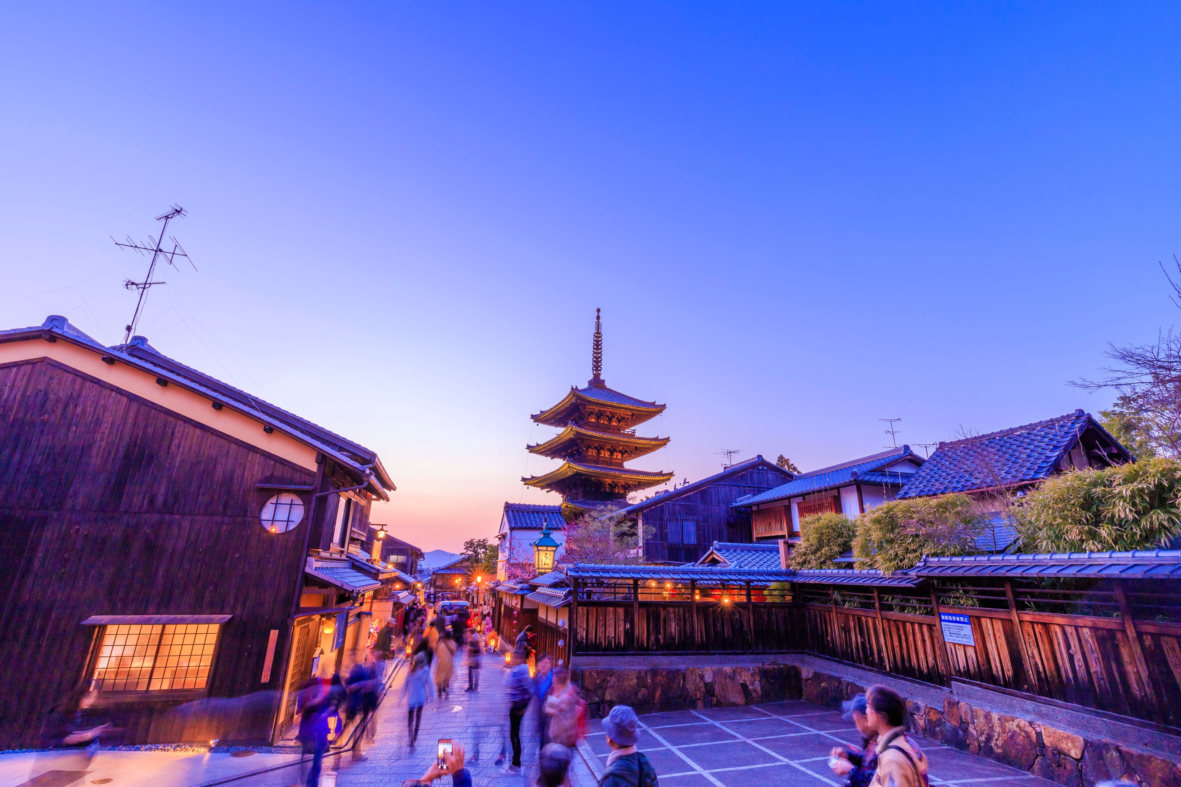 Uma rua tradicional japonesa com edifícios de madeira e uma pagode ao fundo.