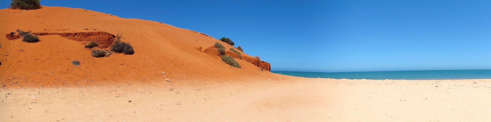 Paisagem desértica com uma praia de areia e vegetação escassa.