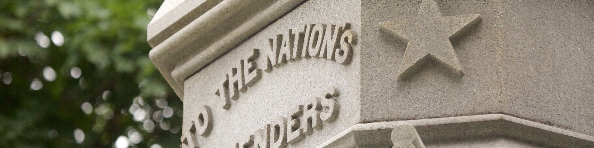 Um monumento de pedra com a inscrição 'Aos Defensores das Nações' e um emblema de estrela.