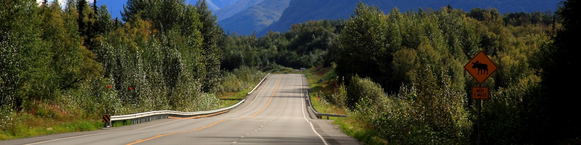 Uma estrada sinuosa serpenteando por montanhas imponentes, ladeada por florestas densas.