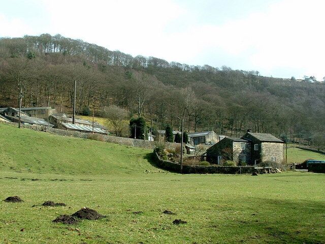 Paisagem rural com casas de pedra, um campo gramado e uma colina ao fundo.
