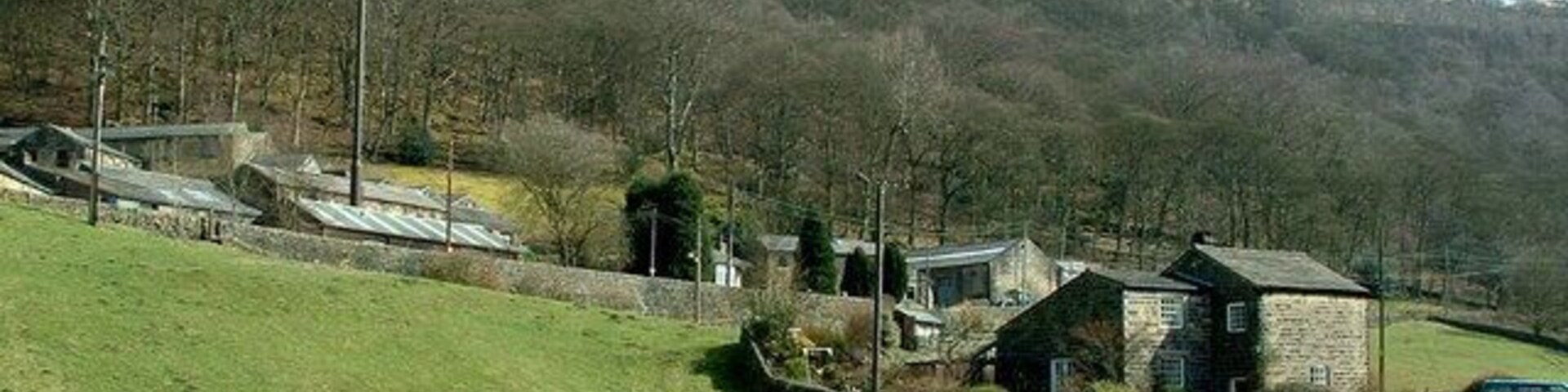 Paisagem rural com casas de pedra, um campo gramado e uma colina ao fundo.
