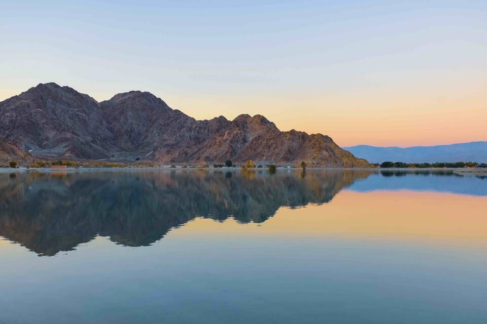 Uma cordilheira refletida em um lago calmo durante o pôr do sol.