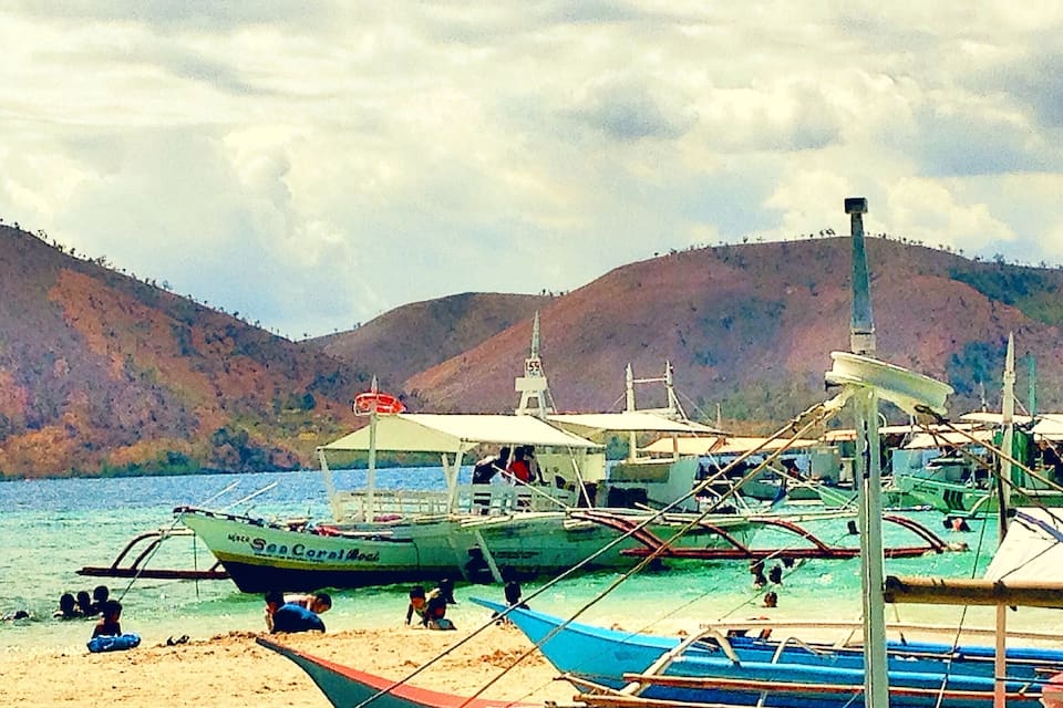 Uma praia com barcos e montanhas ao fundo.