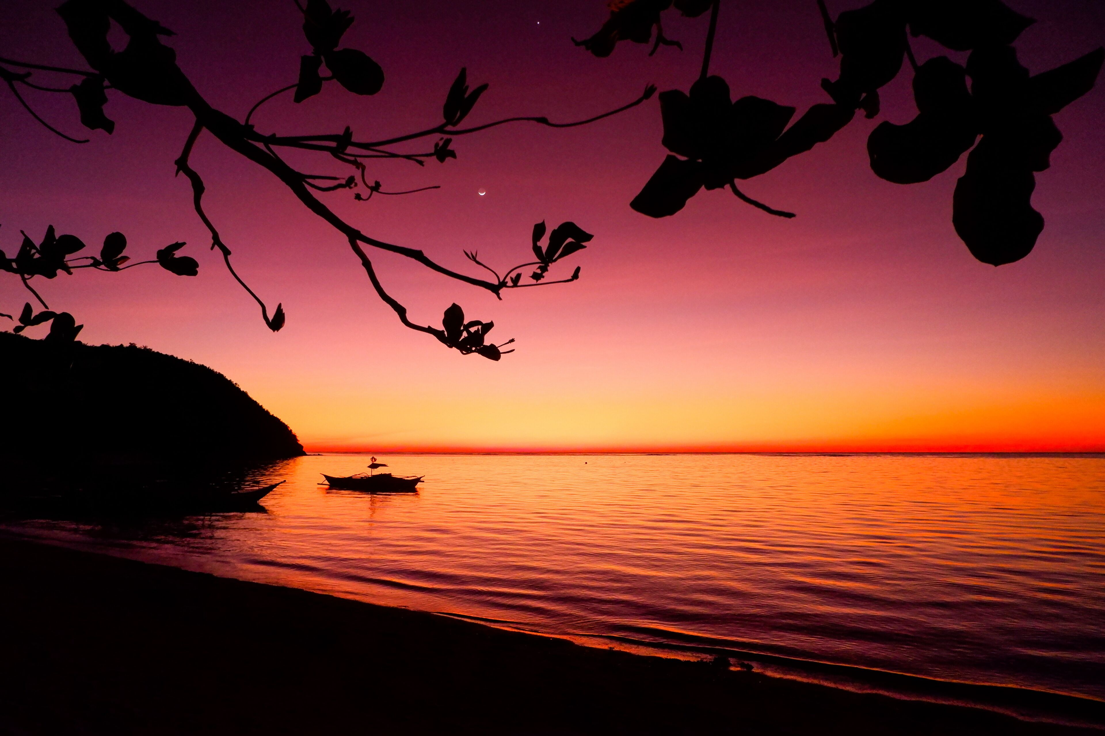 Um pôr do sol sobre um mar calmo, com silhuetas de barcos e um penhasco.