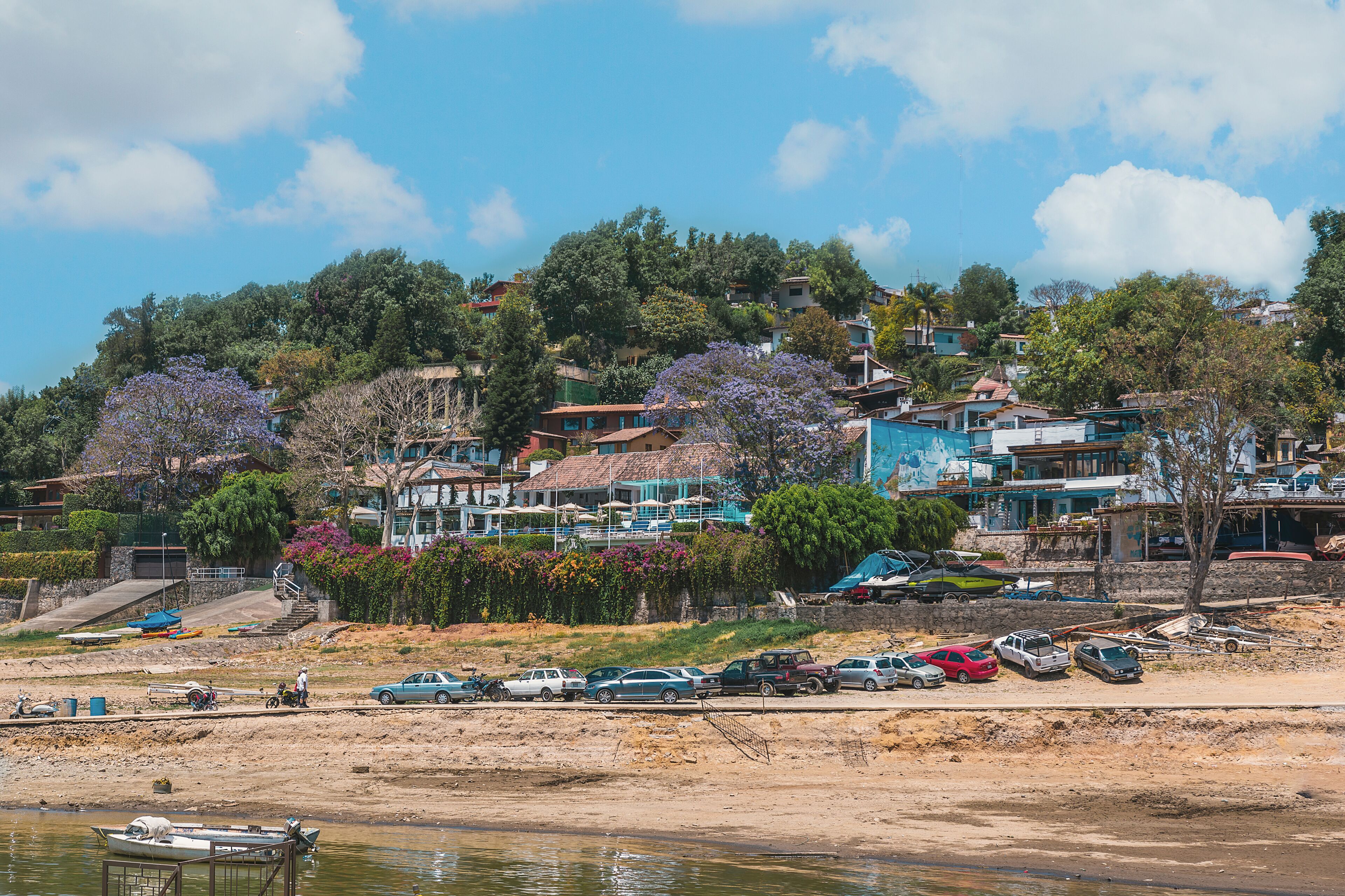 Uma vila costeira com carros estacionados, um barco e casas numa encosta.