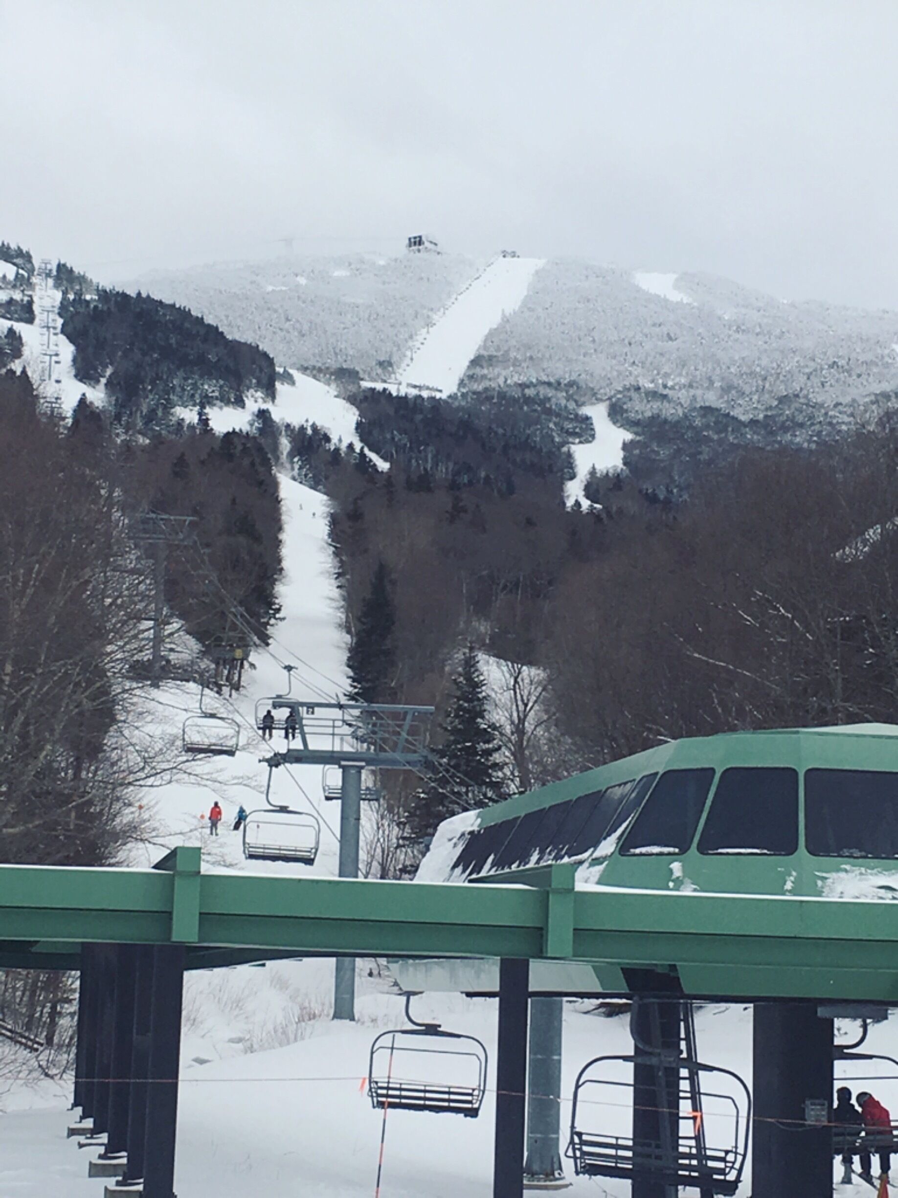 Paisagem montanhosa coberta de neve, com teleféricos e um edifício verde.