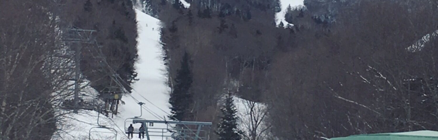 Paisagem montanhosa coberta de neve, com teleféricos e um edifício verde.