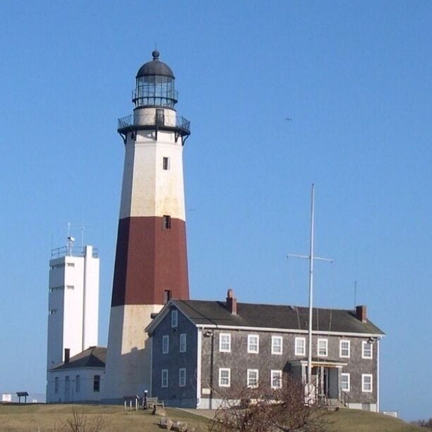 Um farol com torre vermelha e branca, um edifício branco e um mastro de bandeira.