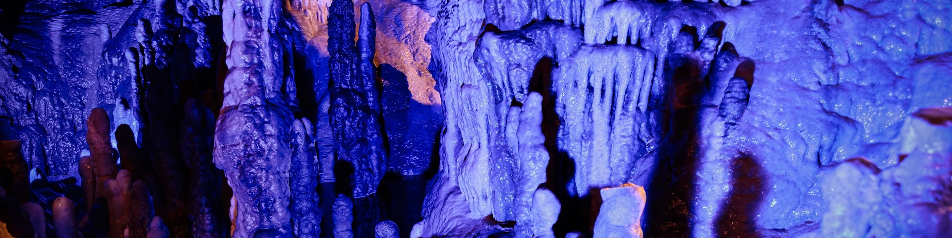 Caverna com estalactites e estalagmites iluminadas por luz azul.