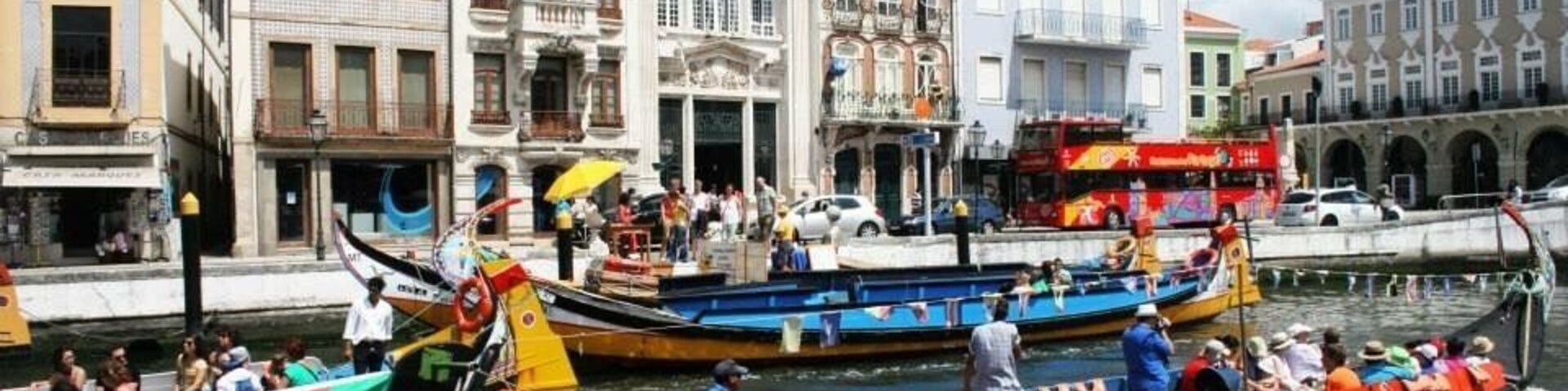 Um desfile de barcos tradicionais em um rio, com espectadores e edifícios ricamente decorados ao fundo.