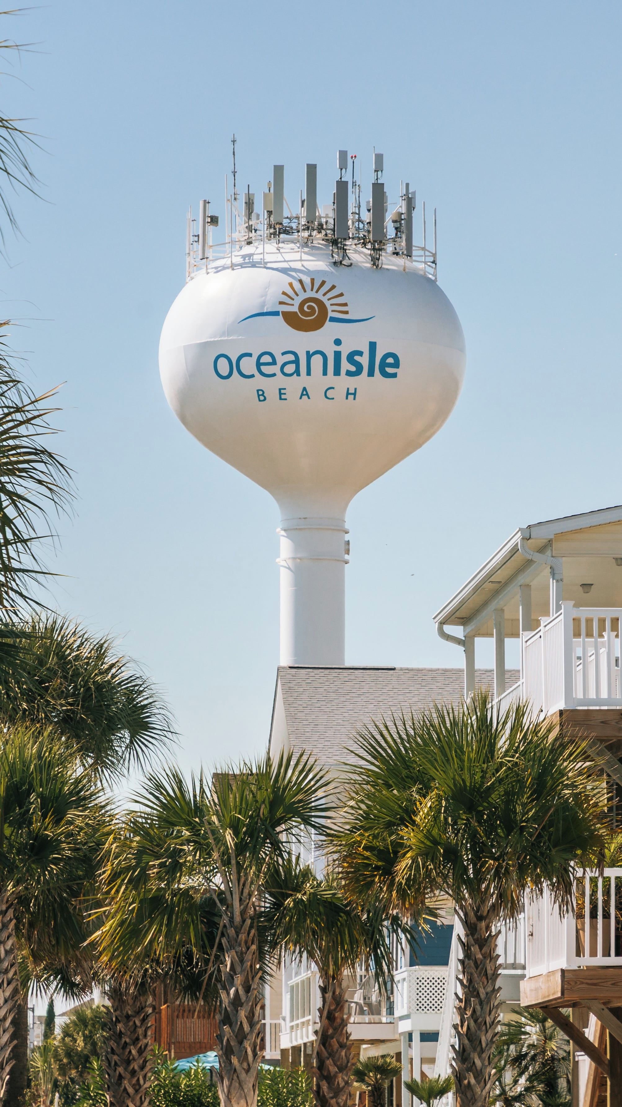 Um tanque de água com o texto 'Oceanisle Beach' e um logotipo, cercado por palmeiras e um edifício com varanda.